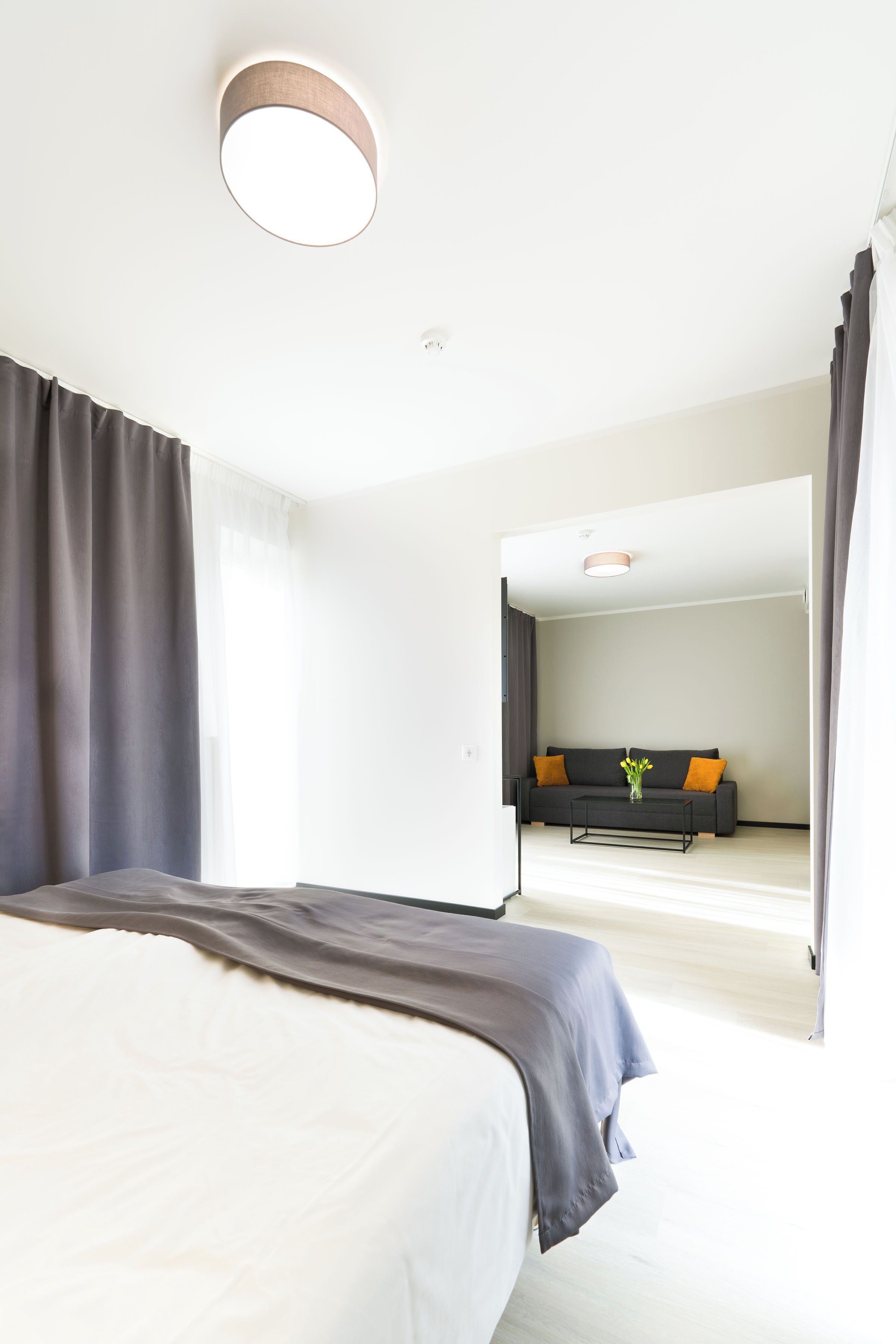 Quarto de hotel moderno com uma cama grande, um sofá na área de estar adjacente e um lustre no teto.