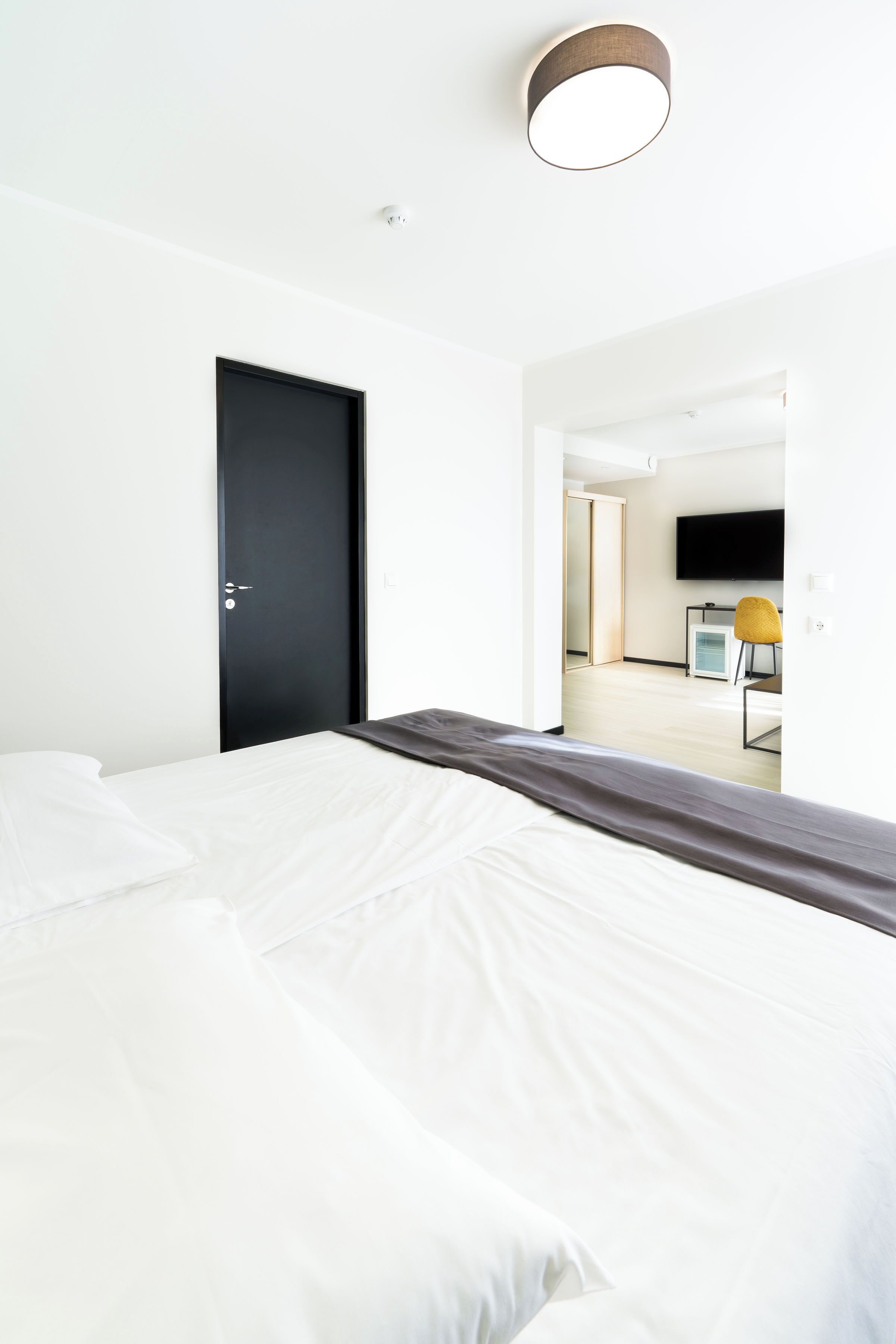 Quarto de hotel moderno com cama, porta preta, televisão de tela plana e pequena escrivaninha com cadeira.