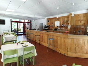 Um restaurante com balcão de madeira, cadeiras verdes e mesas com toalhas brancas.