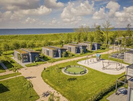 Uma área residencial moderna com casas compactas, um parquinho circular e vista para o mar.