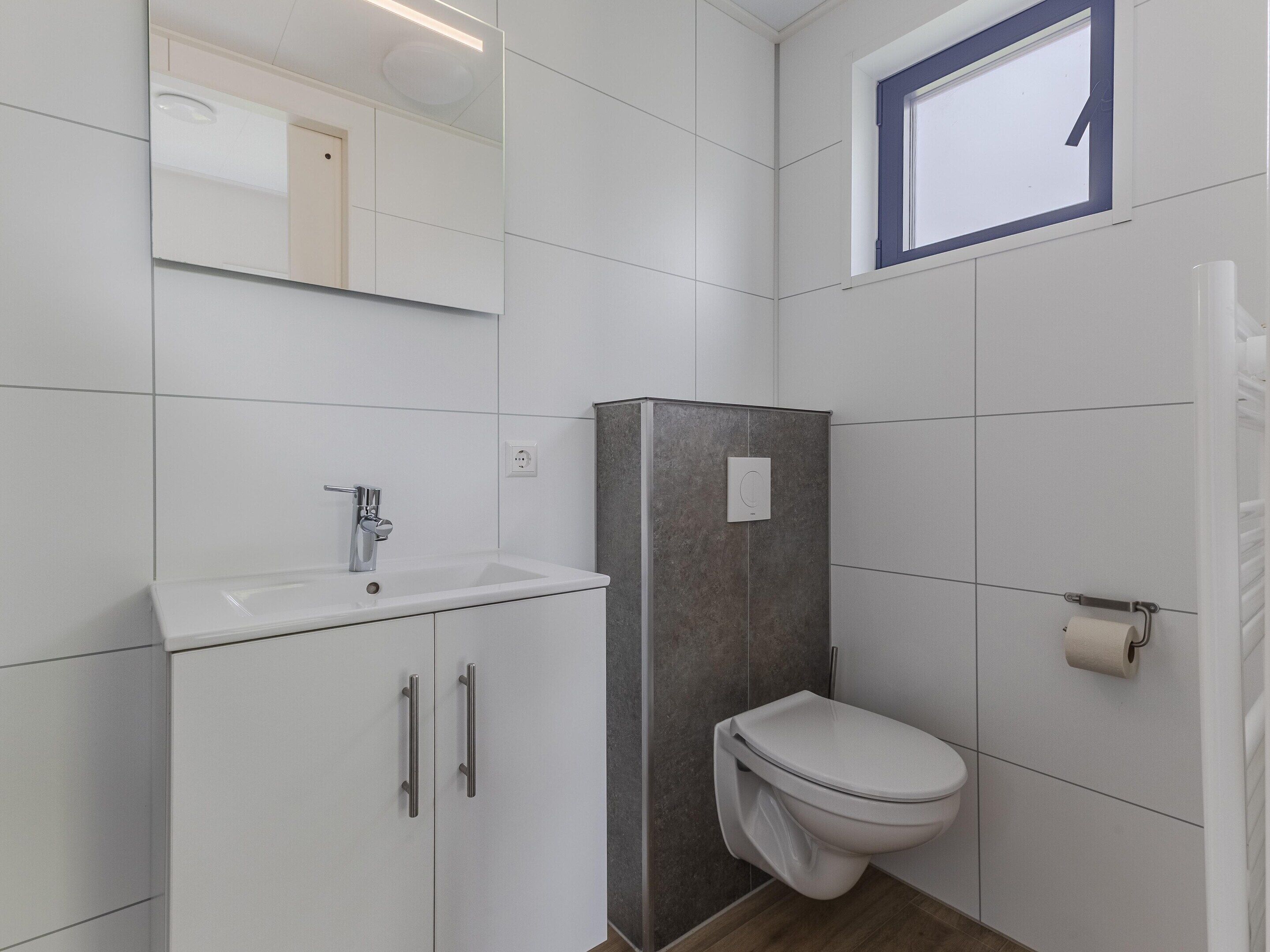 Uma casa de banho moderna com uma sanita, um lavatório e um espelho sobre o lavatório.