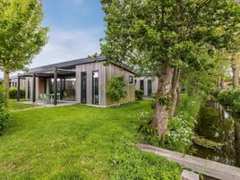 Uma casa moderna com um alpendre coberto, um lago e vegetação exuberante.