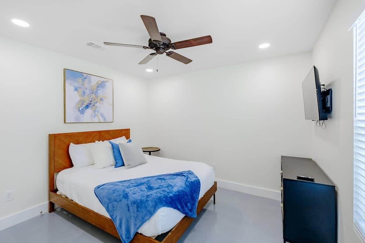 Quarto com cama, ventoinha no teto, quadro, televisão e um pequeno armário.