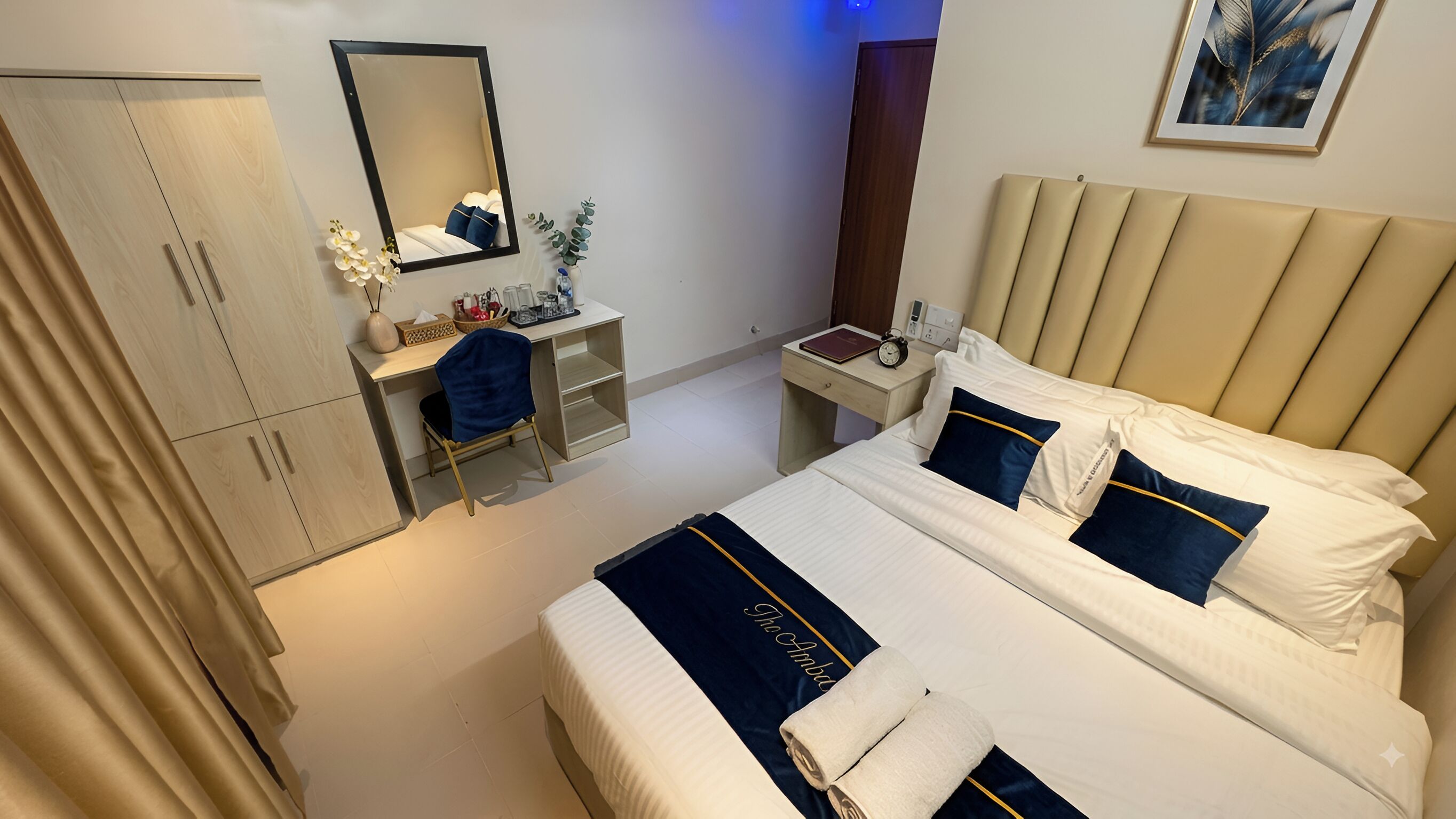 Quarto de hotel com uma cama, escrivaninha, guarda-roupa e espelho.