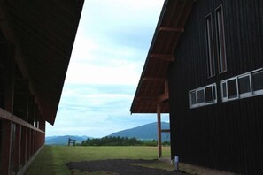 Um edifício com telhado inclinado, grandes janelas e vista para uma área gramada e montanhas ao longe.