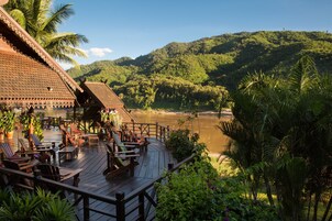 Um deck de madeira com área de estar externa, com vista para um rio e vegetação exuberante.