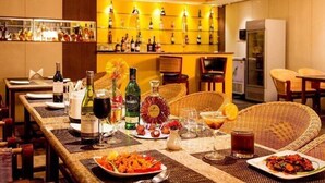 Restaurante com uma longa mesa posta para refeição, diversos vinhos e cadeiras de vime.