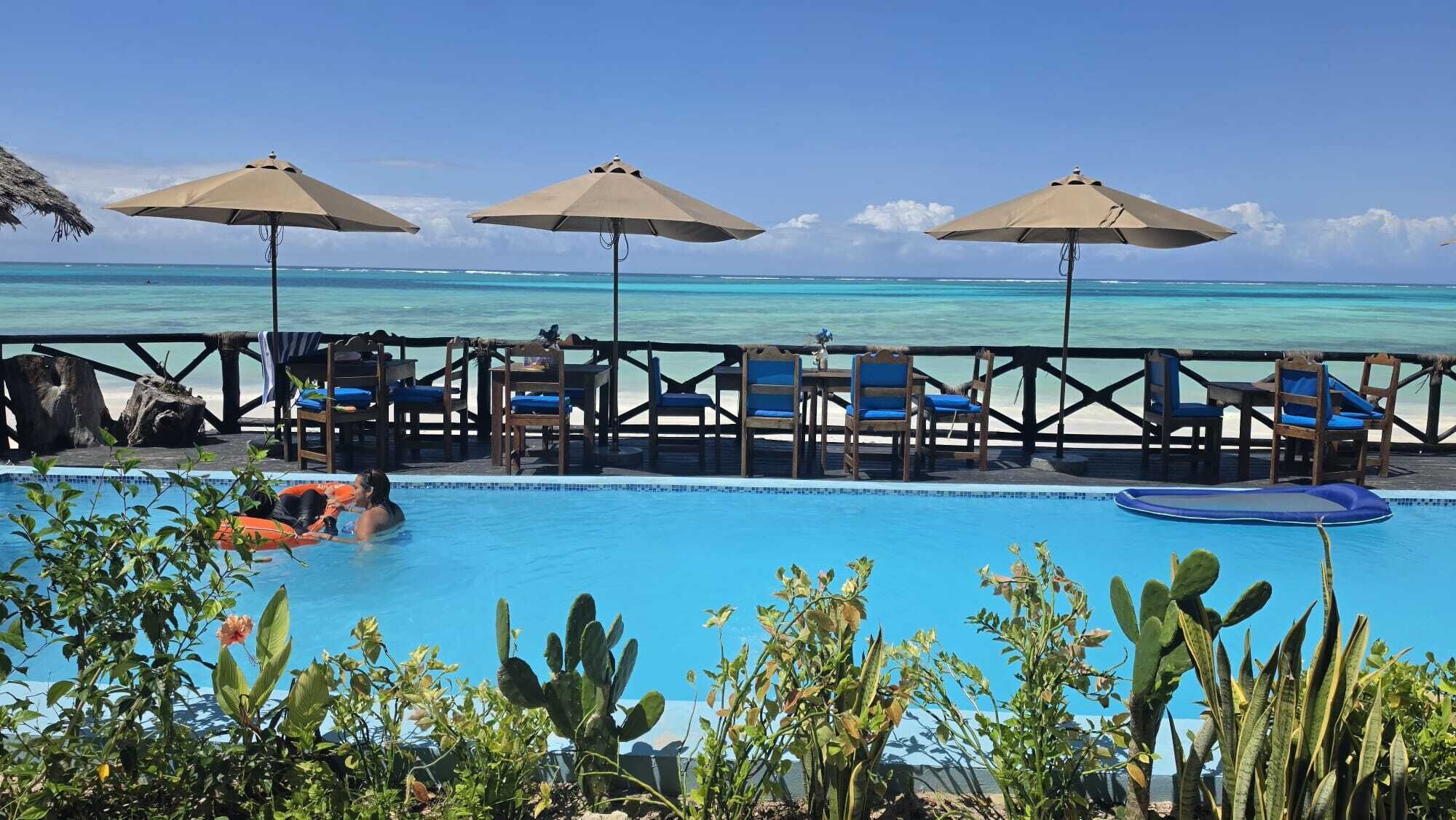 Área de piscina com espreguiçadeiras e guarda-sóis, com vista para um mar azul e límpido.