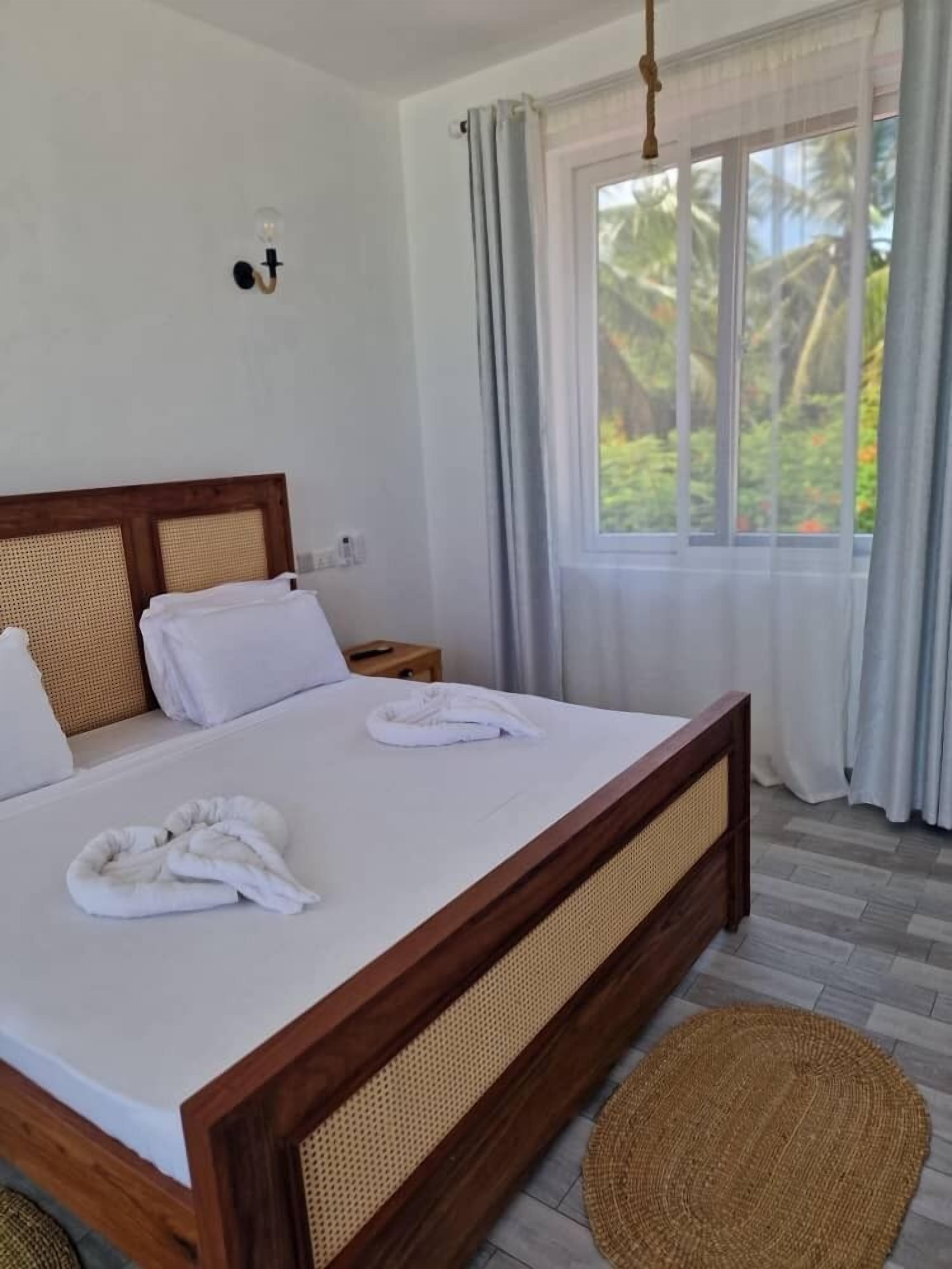 Uma cama com roupa de cama branca, cabeceira de madeira e painel lateral trançado.