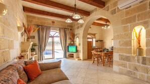 Uma sala de estar ampla com sofá, televisão, paredes de pedra, vigas de madeira e área de refeições.