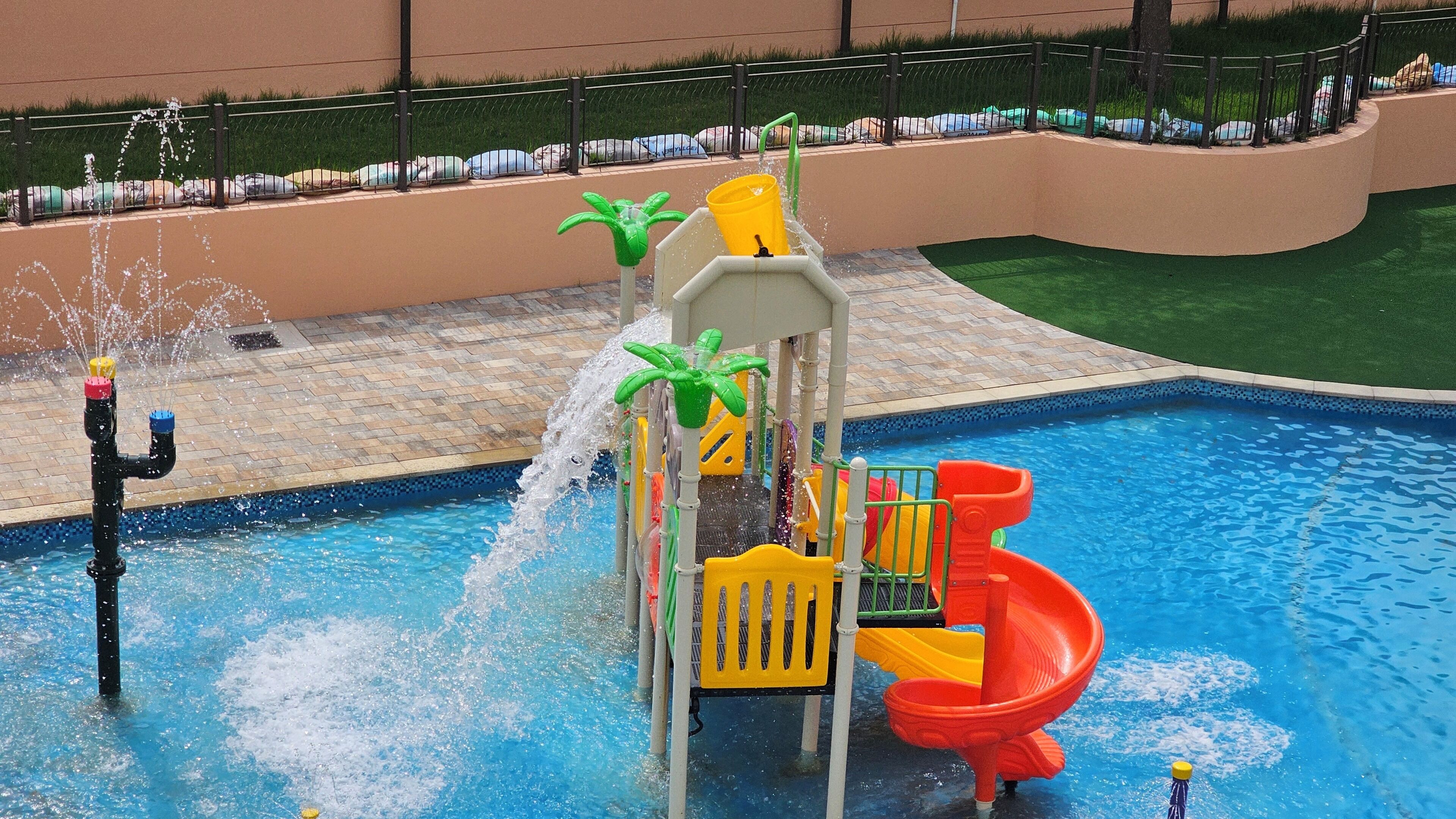 Piscina com área de recreação aquática, incluindo escorrega e fonte de água.