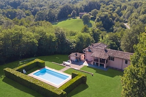 Uma casa com piscina, rodeada por relvados e sebes bem cuidados, situada numa paisagem verdejante e exuberante.