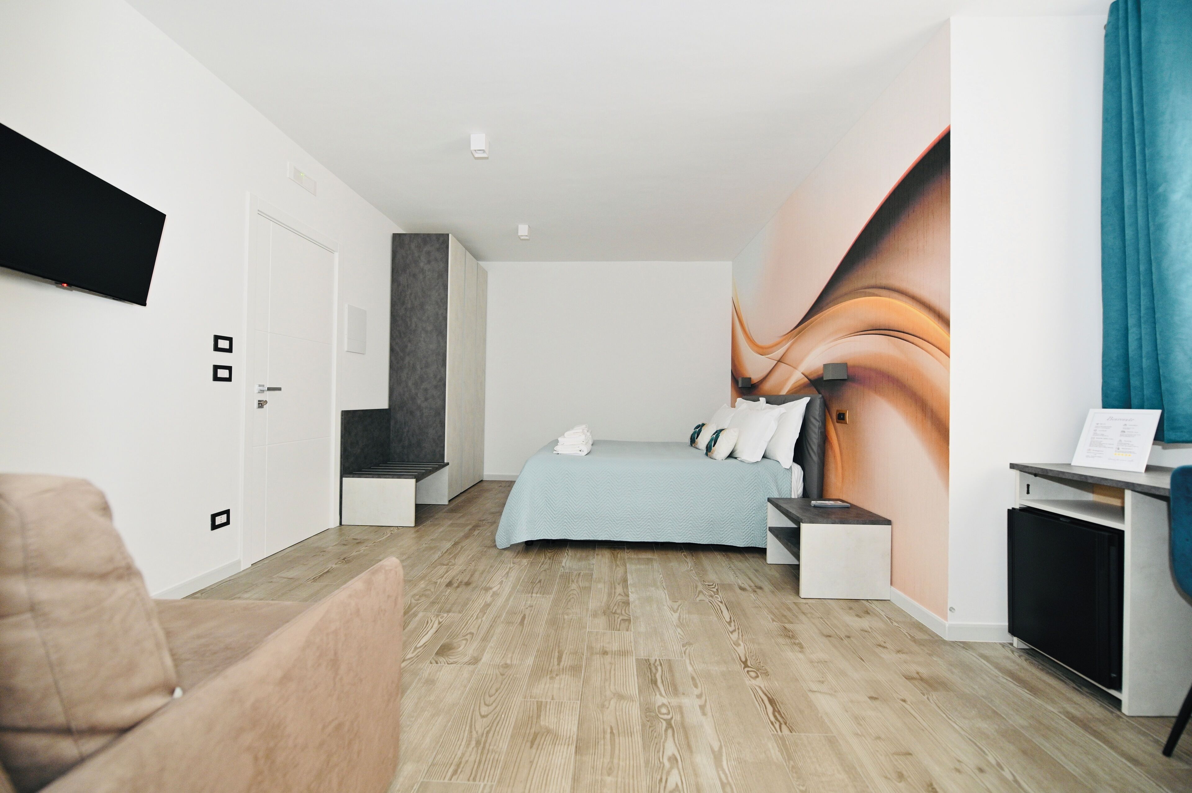 Quarto de hotel moderno com cama, escrivaninha, TV de tela plana e uma grande pintura abstrata na parede.