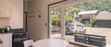 Cozinha moderna com mesa de jantar redonda e cadeiras brancas, uma janela grande com vista para um bairro residencial.