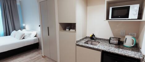 Quarto de hotel compacto com cama, cozinha compacta e pequeno frigorífico.