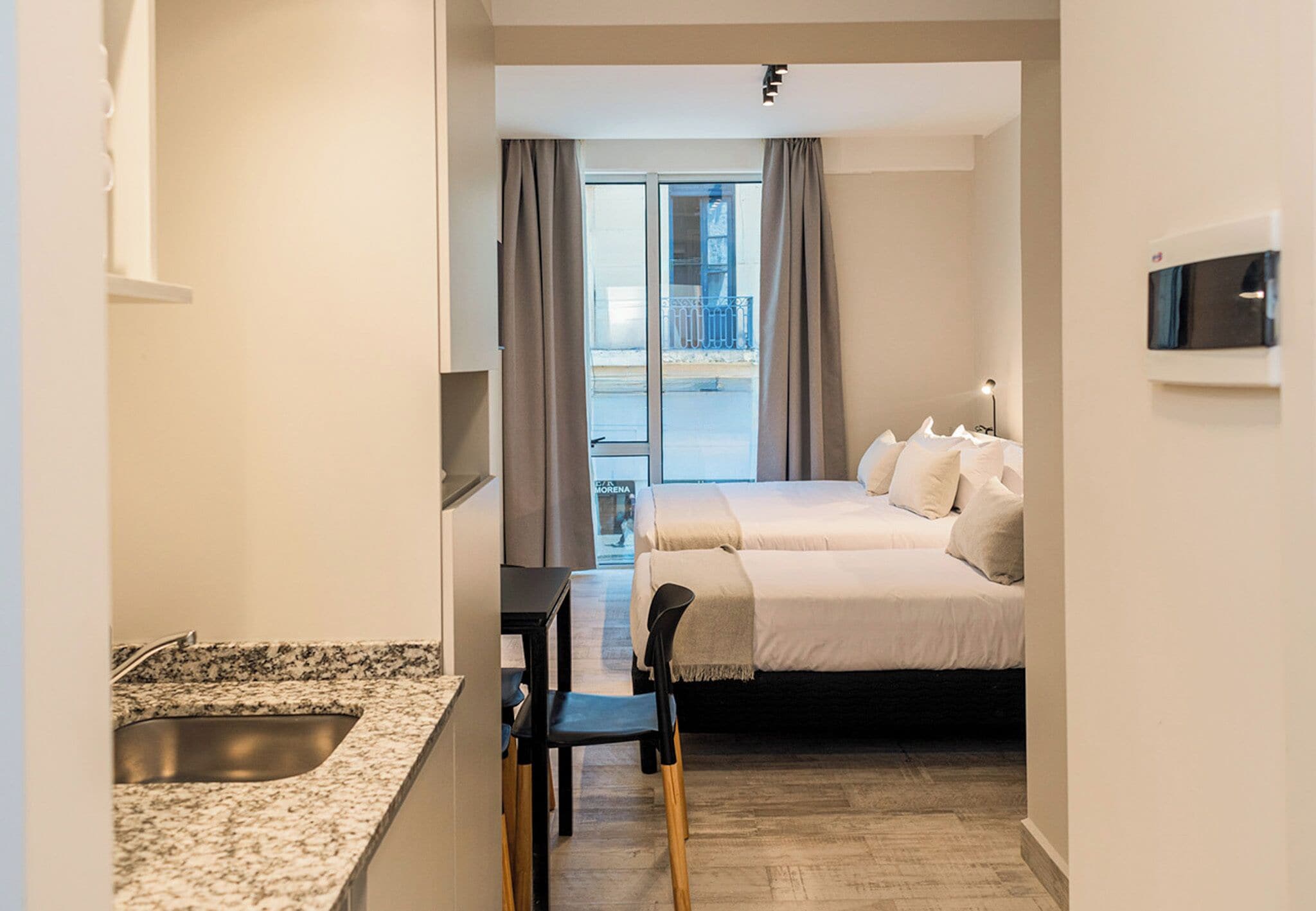 Quarto de hotel com cozinha compacta, uma cama com roupa de cama branca e vista para o exterior por uma porta de correr.