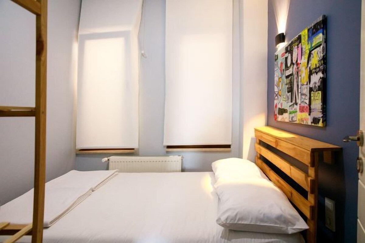 Quarto com cama de madeira, roupa de cama branca, radiador e uma obra de arte pendurada na parede.