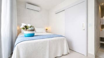Quarto moderno com cama, ar-condicionado branco, abajur e porta para banheiro.