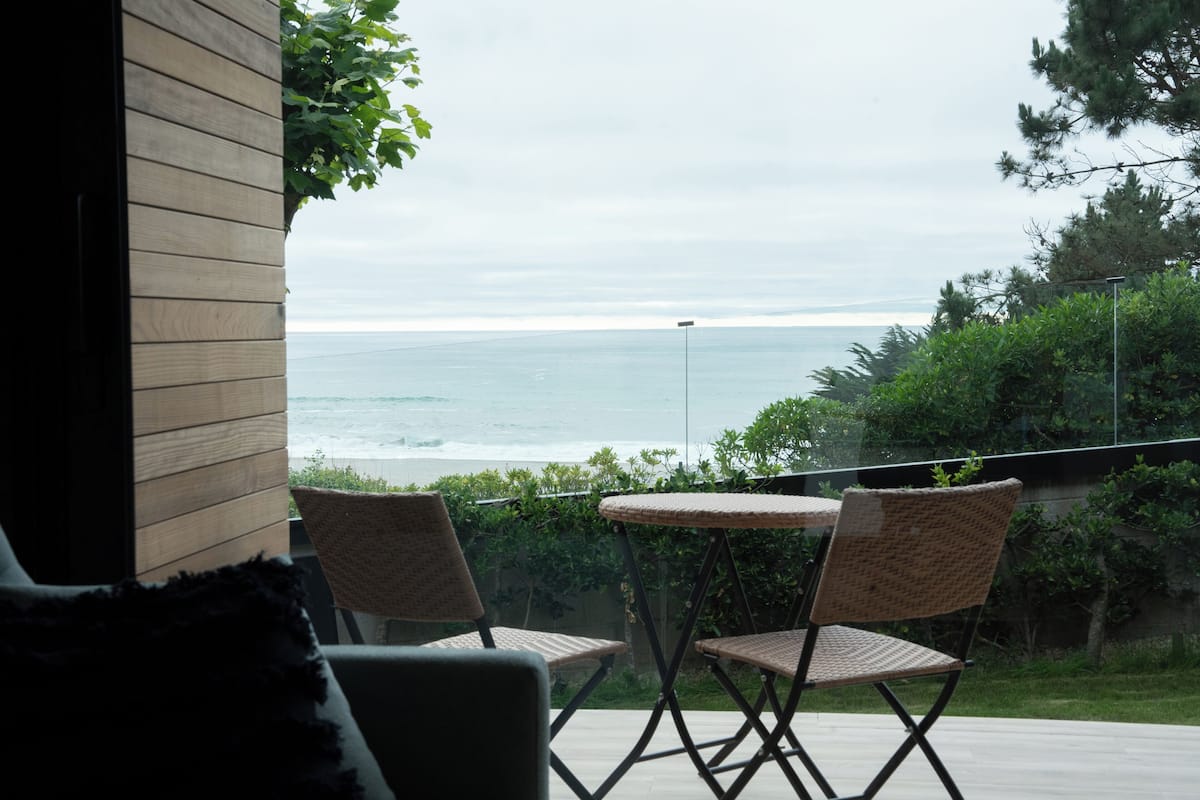 Pátio com duas cadeiras de vime e uma mesa pequena, com vista para a costa.