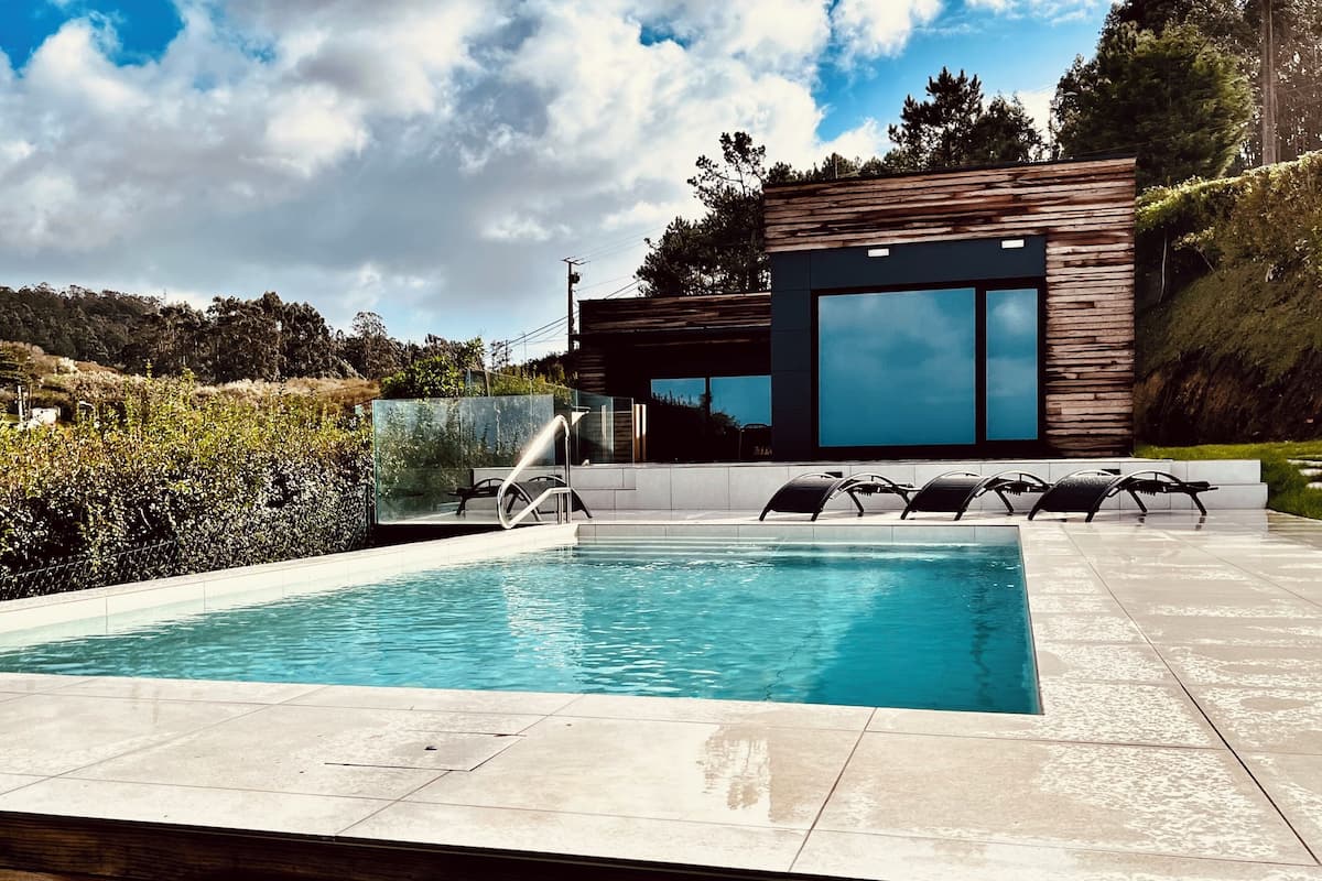Uma área de piscina moderna com uma piscina retangular, espreguiçadeiras e um edifício contemporâneo com amplas janelas.