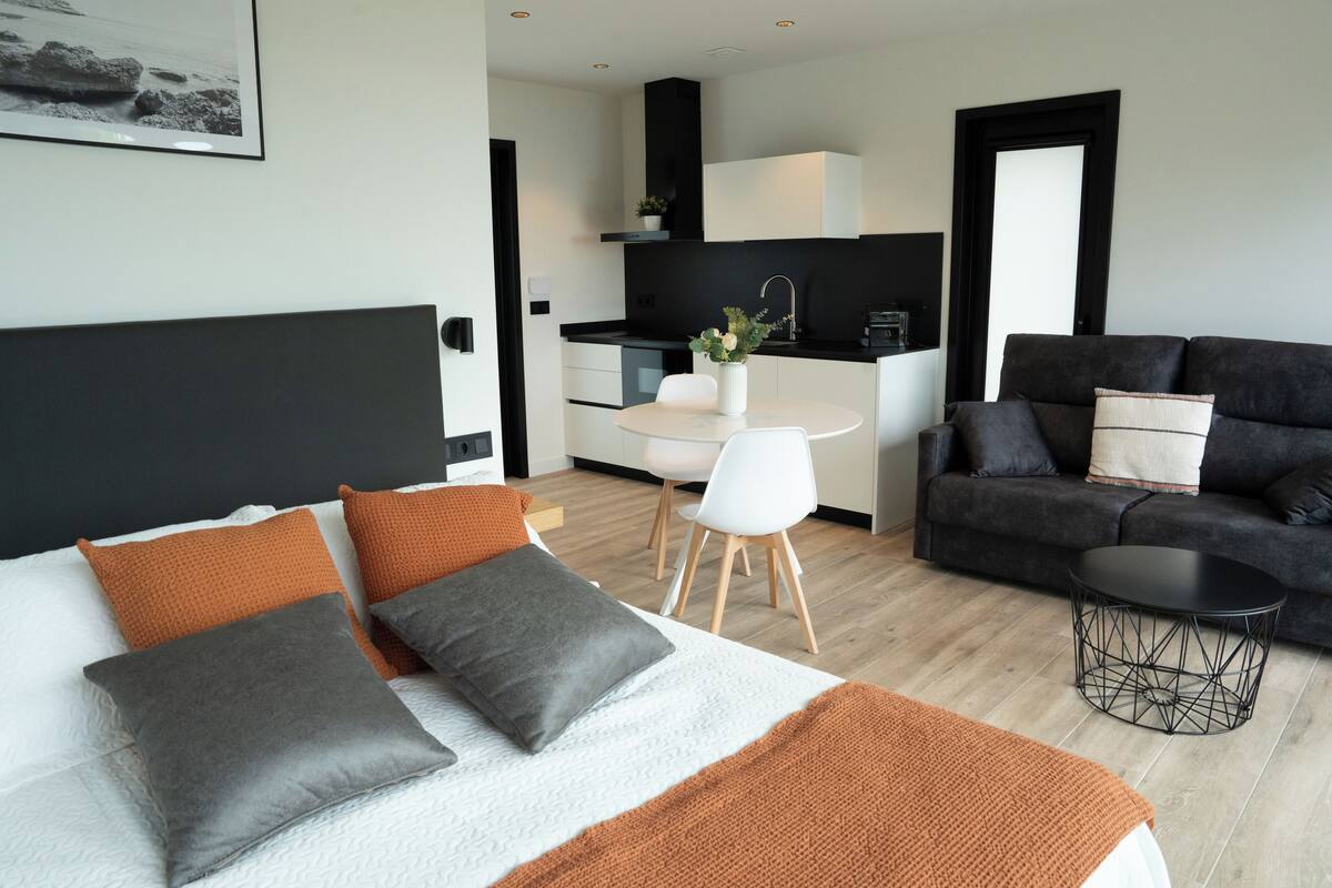 Quarto de hotel moderno com cama, sofá, mesa de jantar e cozinha.