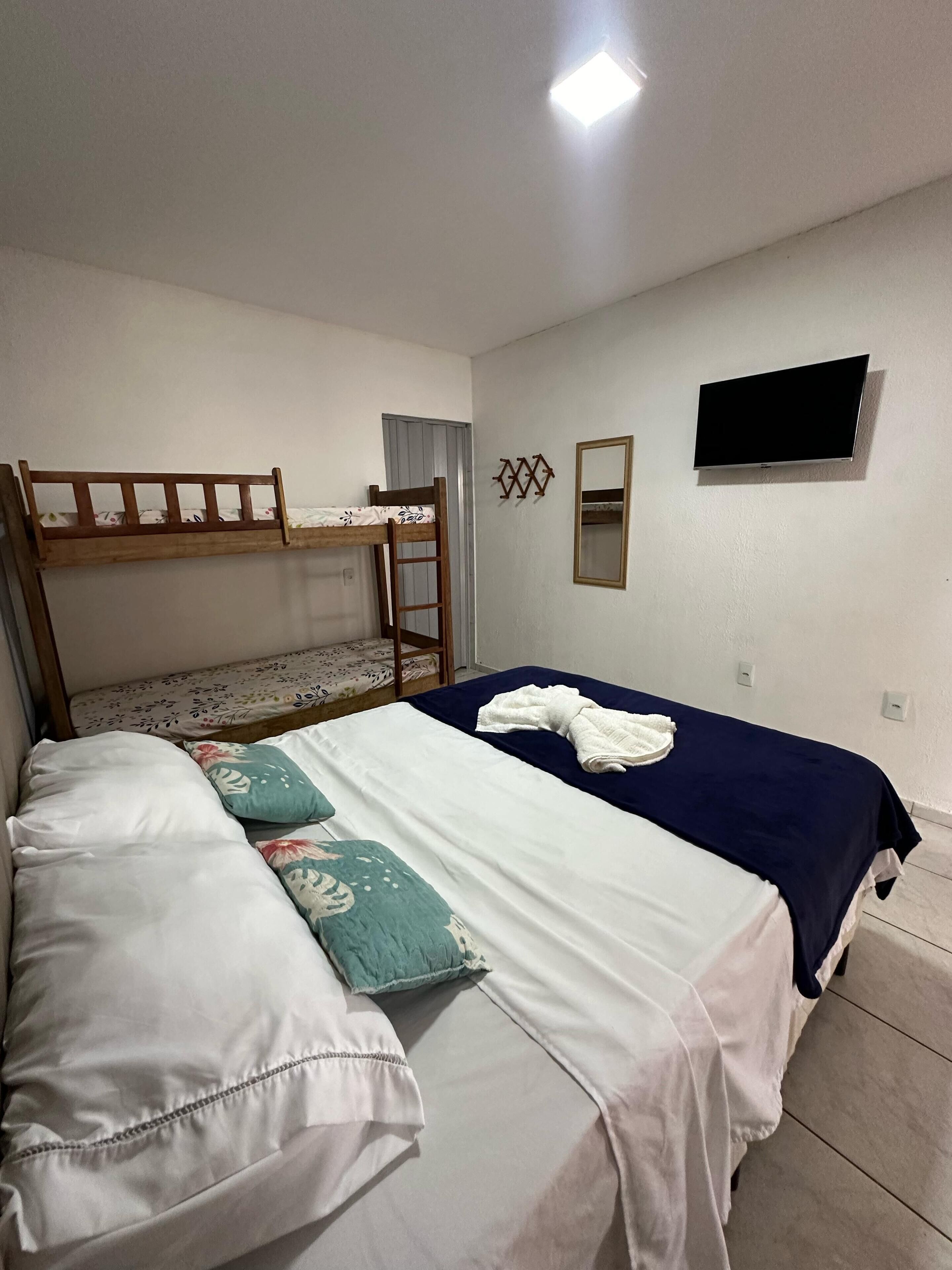 Quarto com uma cama beliche, uma cama de solteiro, uma televisão e um espelho na parede.