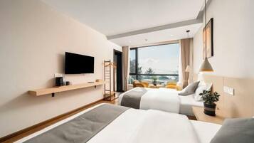 Quarto de hotel com cama, televisão, janela com vista e uma pequena mesa com uma planta.
