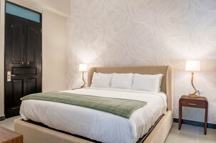 Quarto de hotel com cama, duas luminárias de cabeceira, mesa de cabeceira e papel de parede estampado.