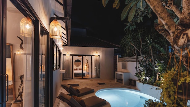 Uma área de piscina moderna ao ar livre, com espreguiçadeiras e um espaço interior bem iluminado com uma cama e cortinas.