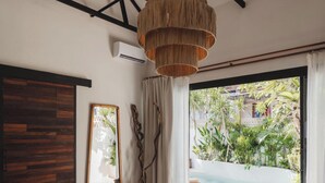 Quarto com cama grande, teto de madeira, luminária pendente, janela com cortinas e vista para piscina e vegetação lá fora.
