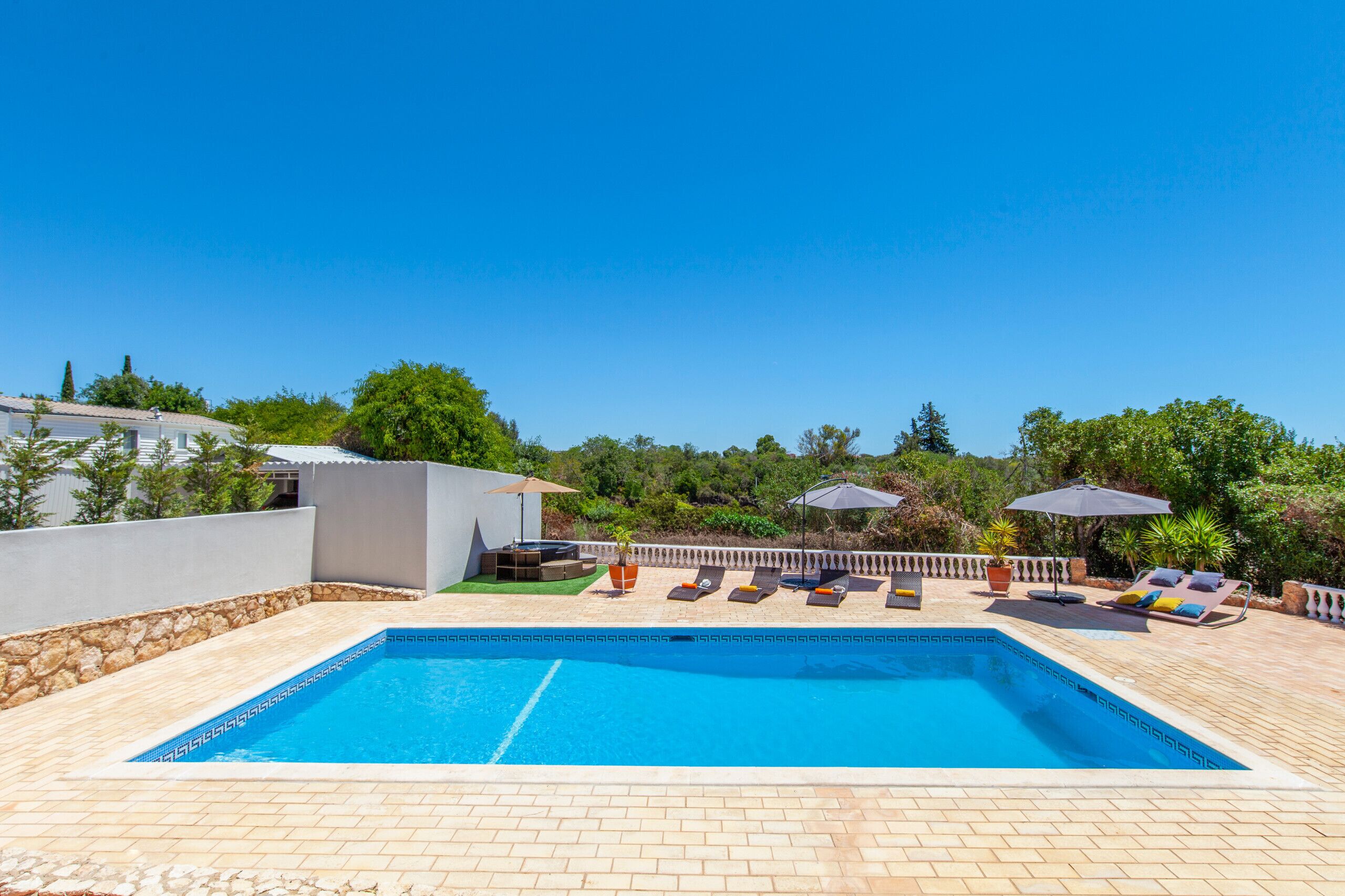 Uma piscina retangular com borda azulejada, rodeada por espreguiçadeiras e guarda-sóis.
