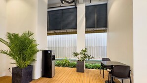 Um espaço interno moderno com piso de madeira, assentos pretos e plantas em vasos.