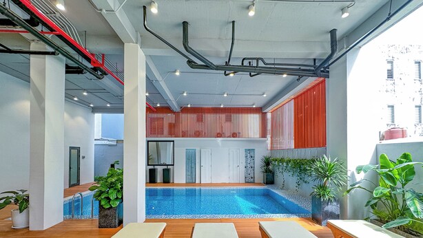 Piscina interna com espreguiçadeiras de madeira, piso ladrilhado e plantas em vasos.