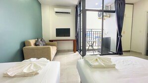 Quarto de hotel com duas camas, um sofá, uma televisão, ar condicionado e uma varanda com vista.