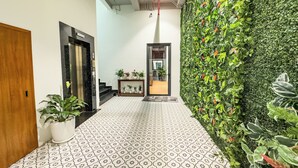 Um corredor com piso estampado, uma porta de madeira, um console com plantas e uma parede verde com folhagem.