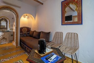Um quarto aconchegante com um sofá, duas cadeiras de vime, uma mesa de centro com um controle remoto e um espelho decorativo.