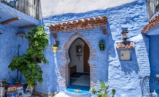 Um edifício tradicional com paredes azuis, entrada em mosaico, planta pendente e uma pequena varanda.