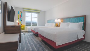 Quarto de hotel com duas camas, uma escrivaninha, televisão, janela com vista e uma luminária.