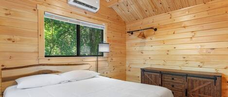 Quarto de cabana de madeira com cama, janela e armário.