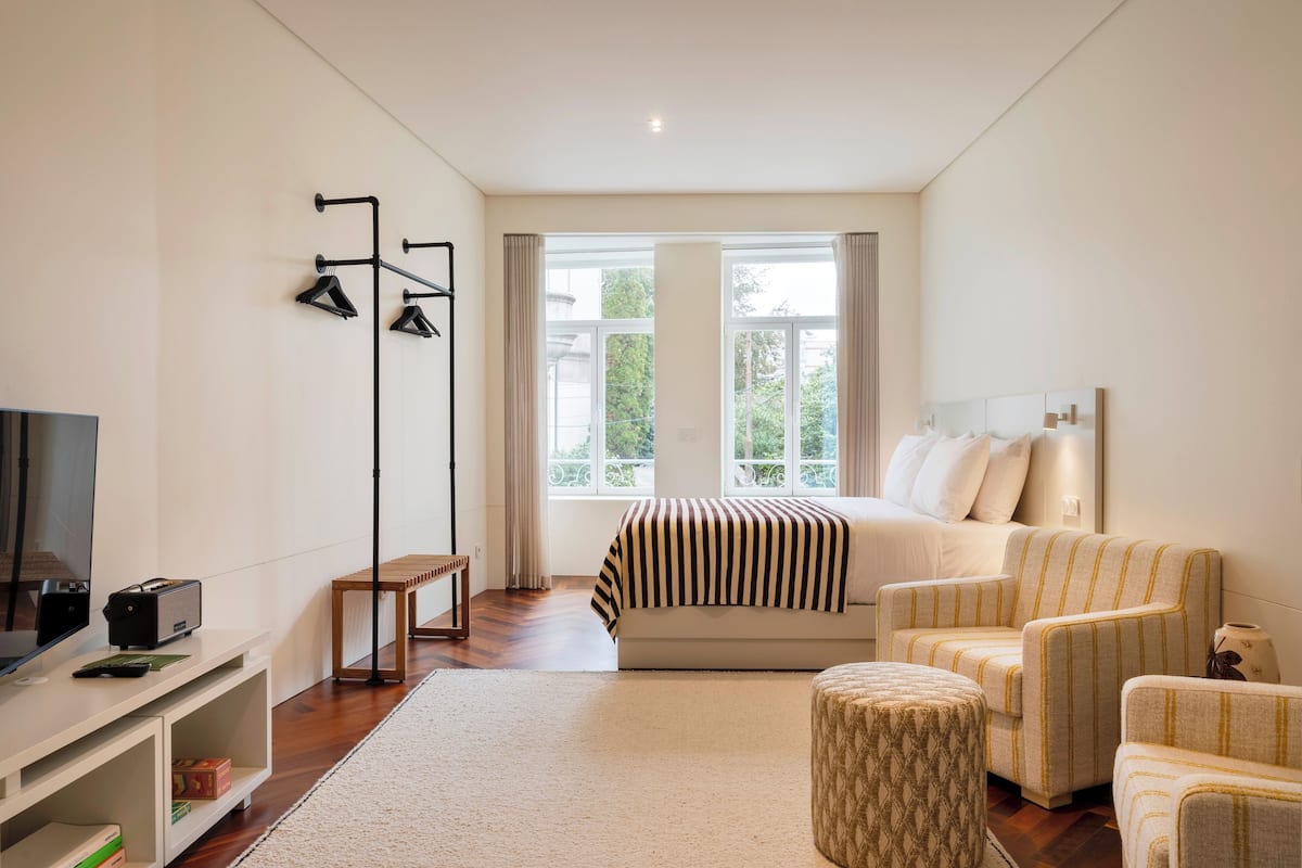 Quarto moderno com cama, televisão, escrivaninha e janela com cortinas.