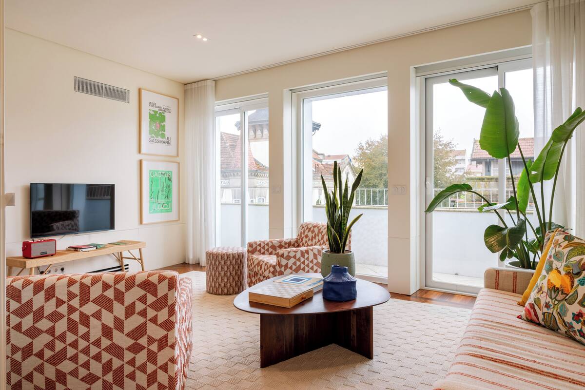 Uma sala de estar moderna com TV, sofá, mesa de centro e janelas amplas.