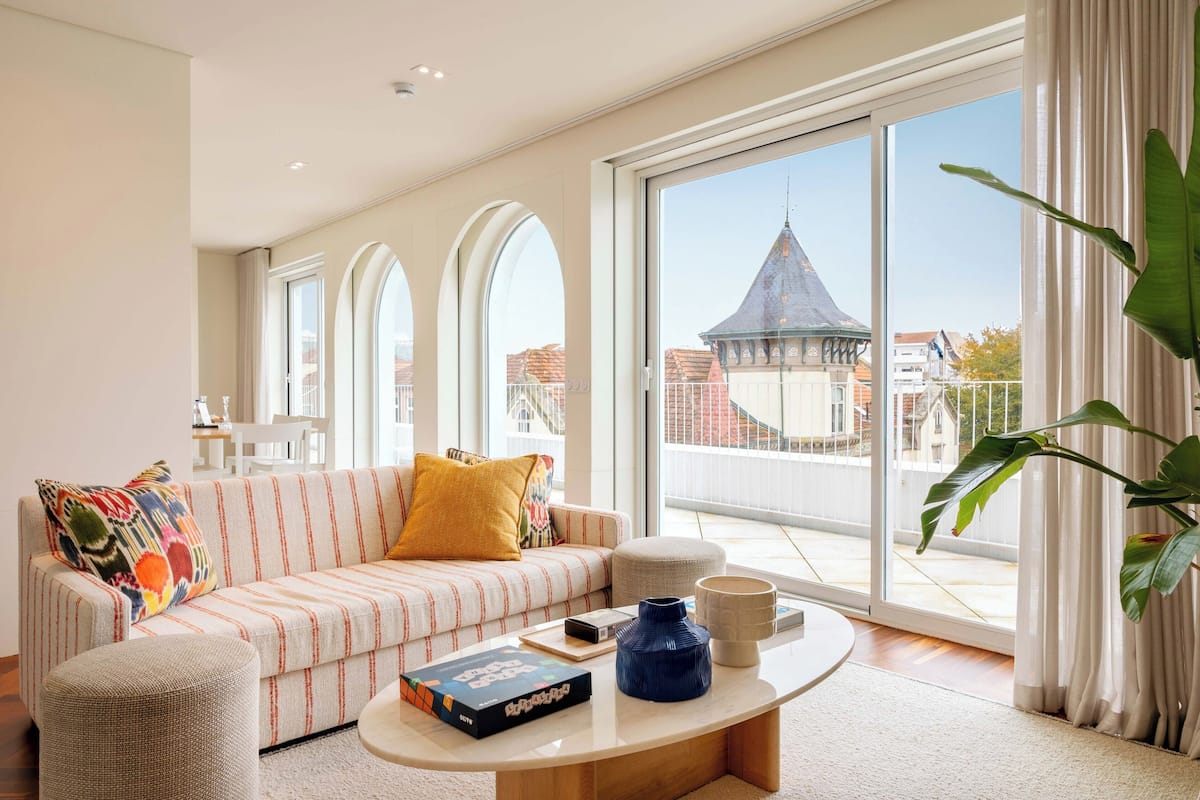Uma sala de estar moderna com um sofá, uma mesa de centro e vista para um horizonte urbano através de grandes janelas.