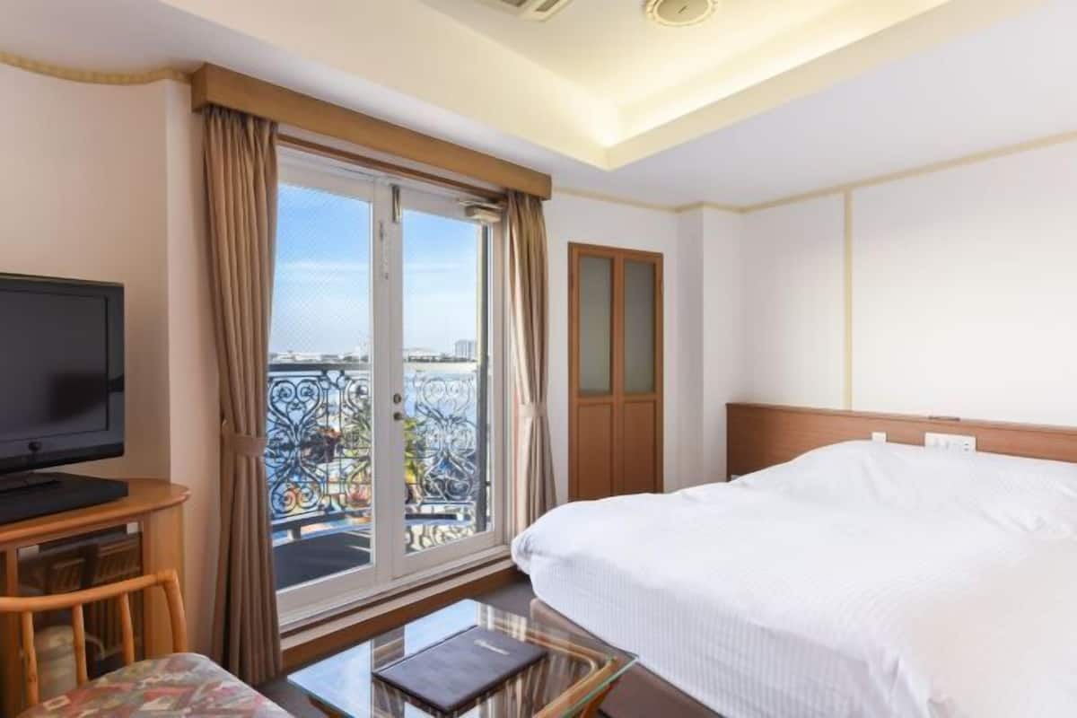 Quarto de hotel com cama, televisão, escrivaninha e varanda com vista.