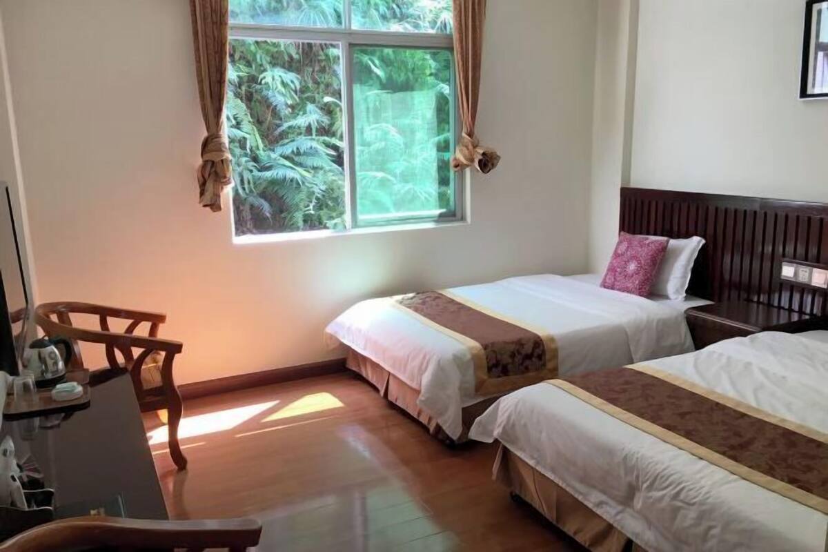Quarto de hotel com duas camas, uma escrivaninha de madeira e uma janela com cortinas.