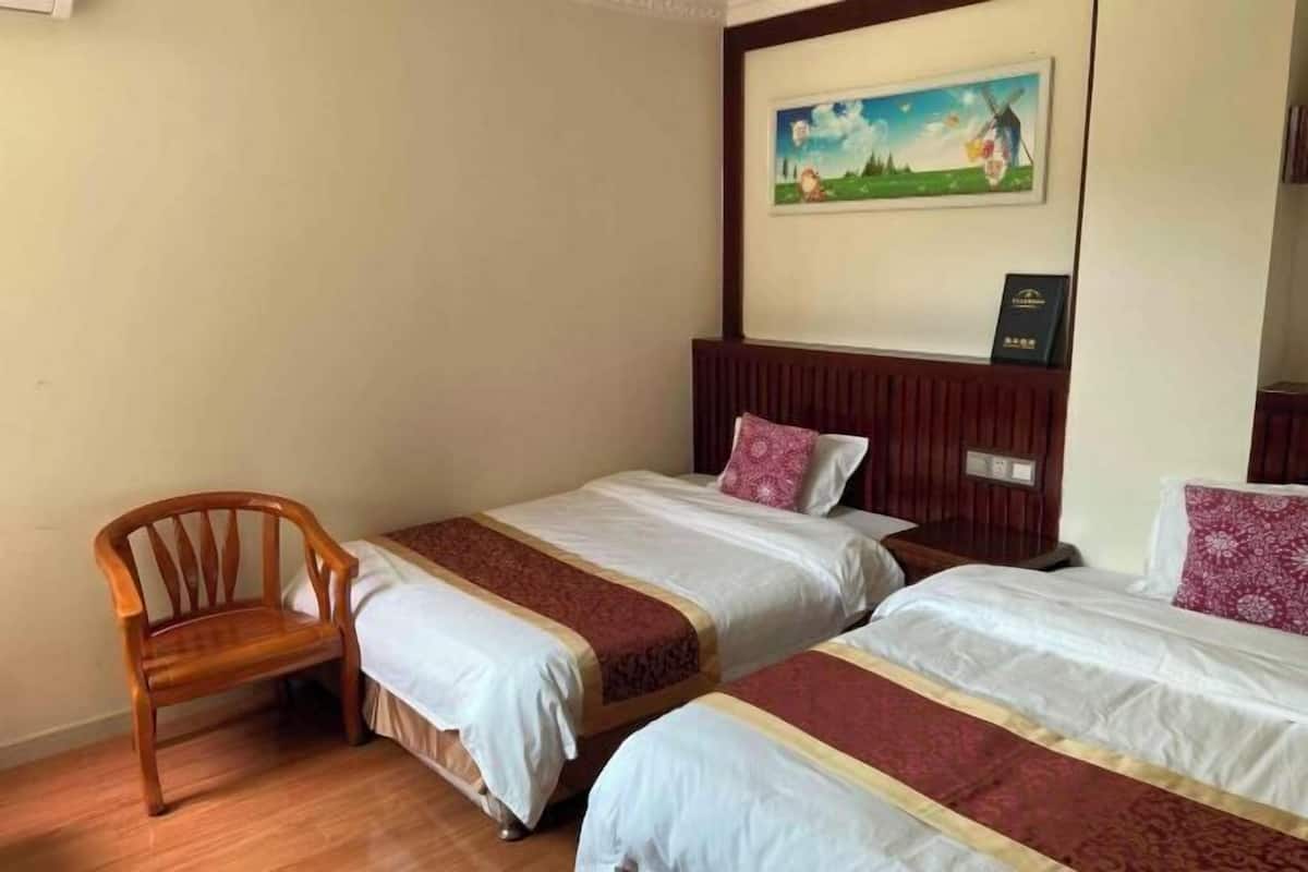 Quarto de hotel com duas camas, uma cadeira de madeira e um quadro na parede.