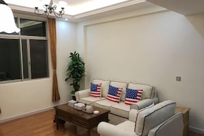 Uma sala de estar com sofá, mesa de centro, planta em vaso e janela com cortinas.