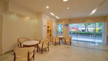 Um saguão de hotel com disposição de assentos, balcão de recepção e vista para o exterior.