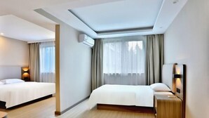 Quarto de hotel com duas camas, uma janela grande com cortinas, ar condicionado fixado na parede e uma mesa de cabeceira com abajur.