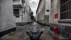 Um beco estreito com um hidrante vermelho à direita, um banco de concreto no centro e edifícios em ambos os lados.