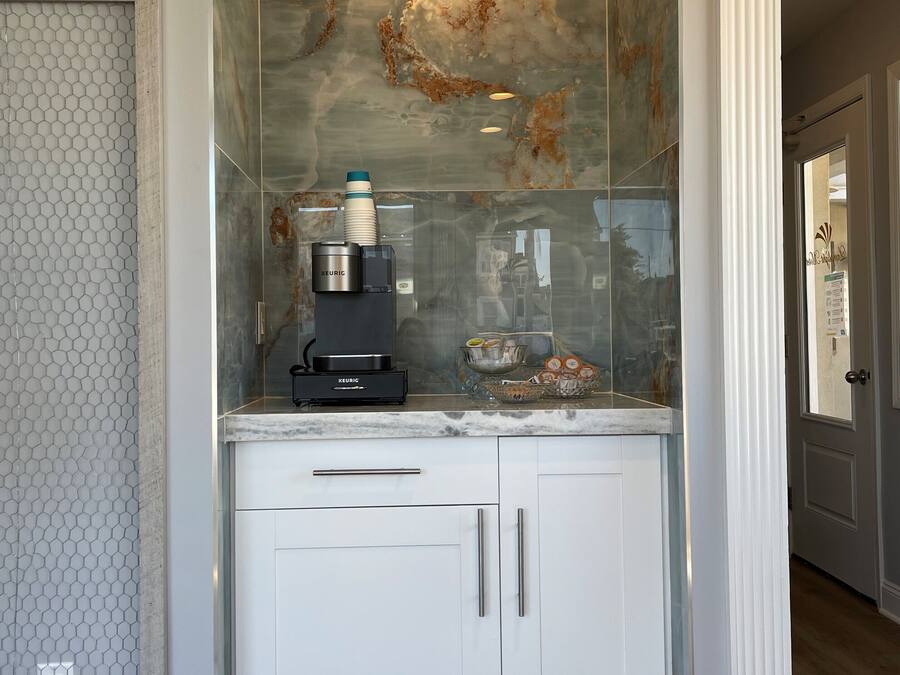 Uma cozinha com máquina de café expresso embutida, armários brancos e painel de fundo de mármore.